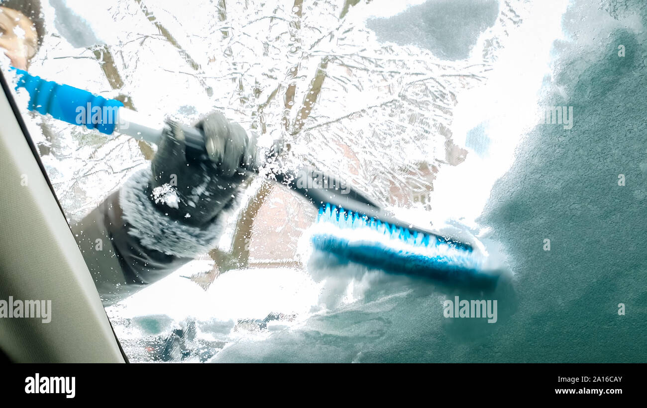 Close up image inside the snow covered car. Smiling lady clean up the ...