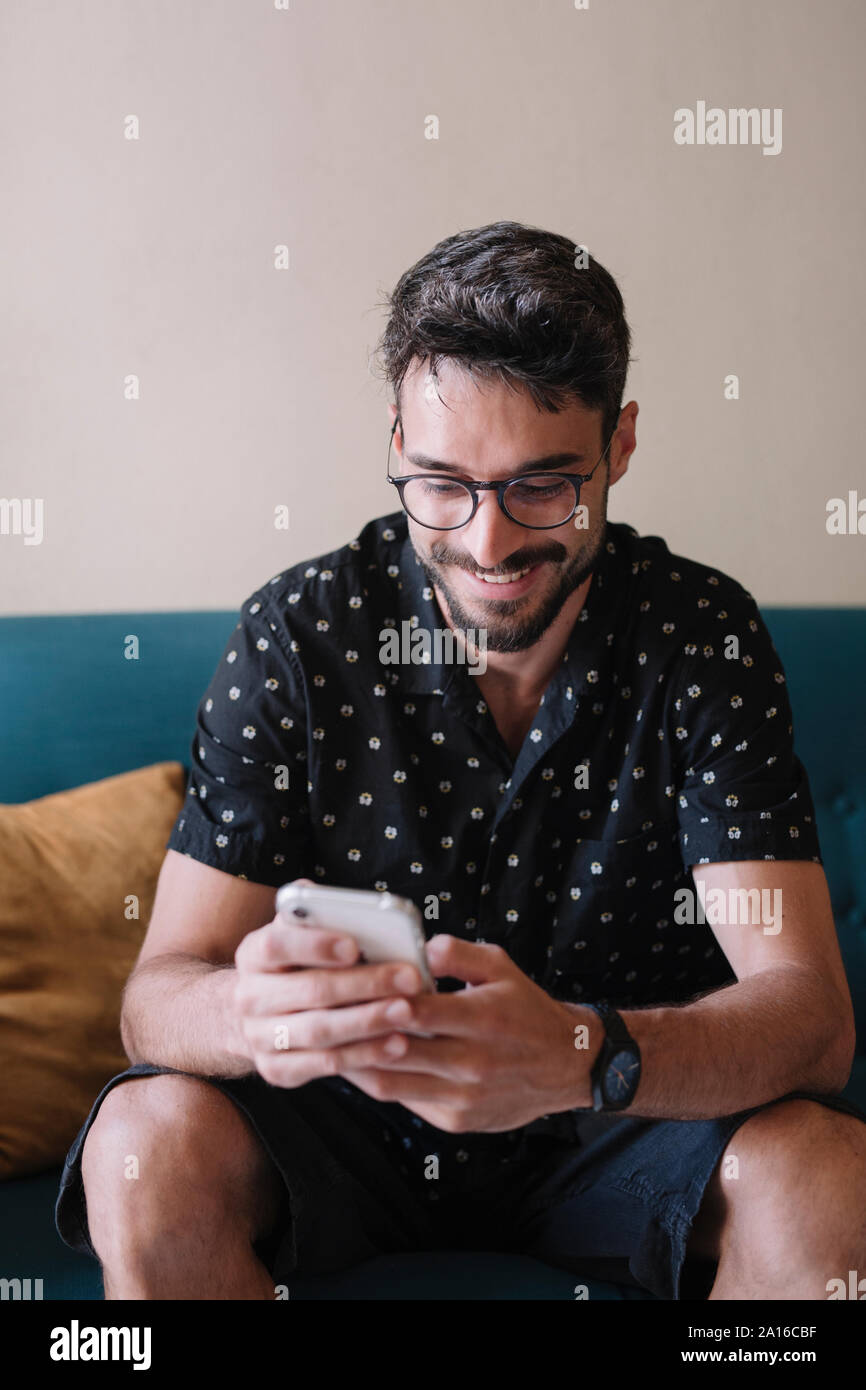 Smiling man sitting on a couch using cell phone Stock Photo - Alamy