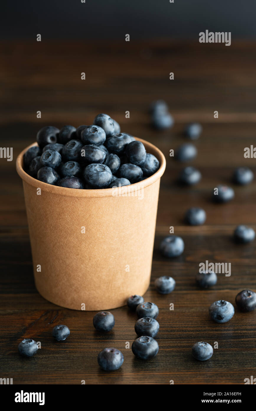 Fresh organic blueberries in a paper cup. Dark wooden table, high ...