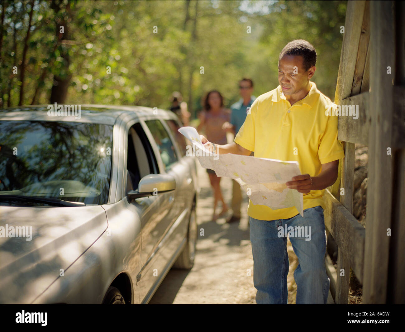 Mid-adult man standing beside a car looking at a map with friends ...