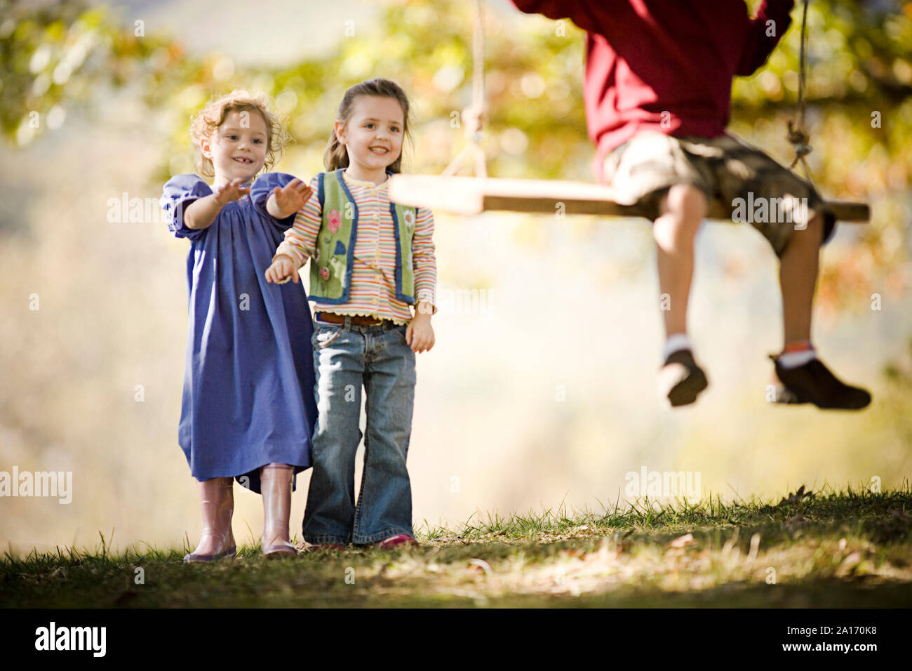 Girls pushing boy on a swing Stock Photo - Alamy