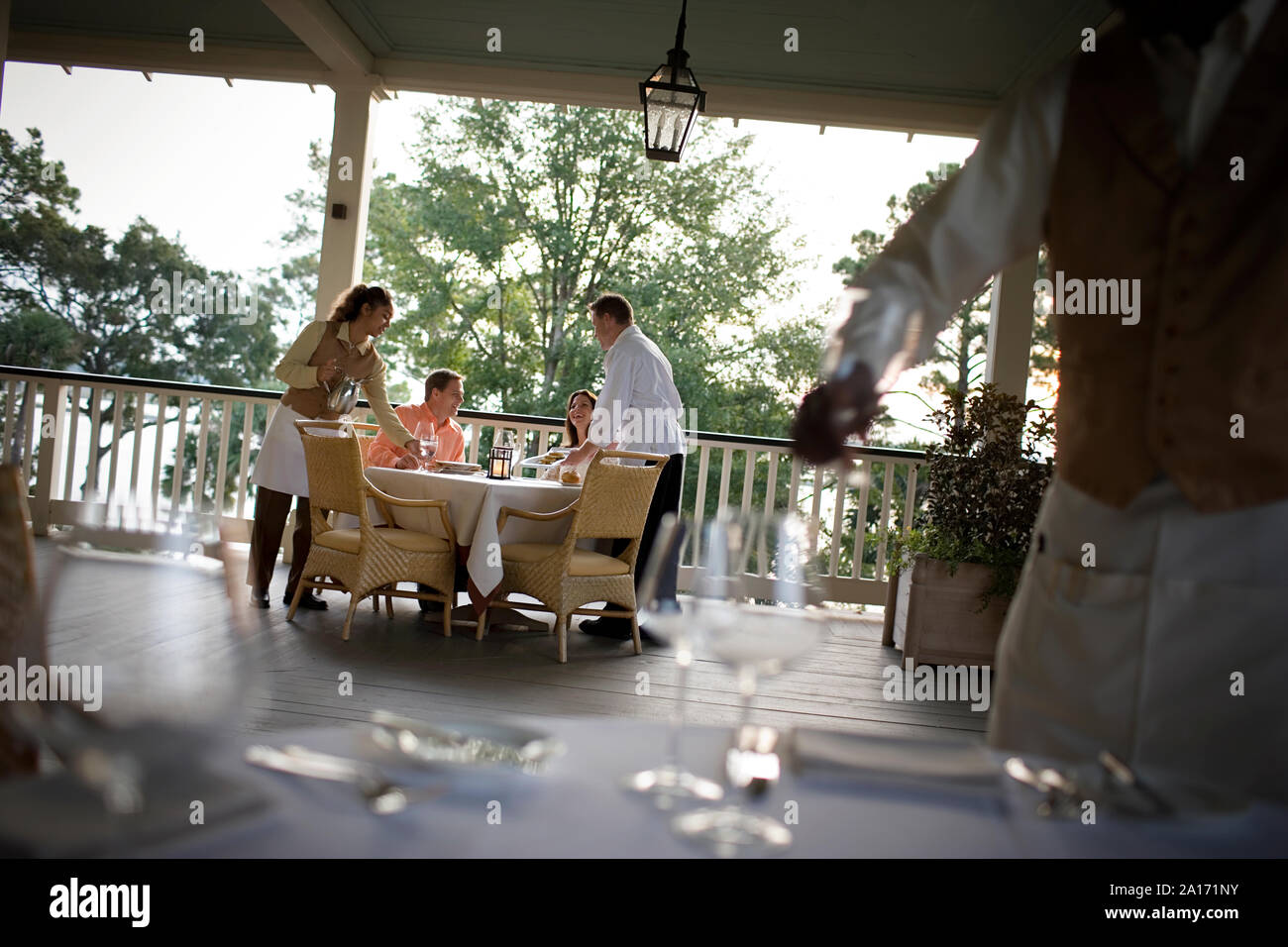 Happy mid-adult couple being served by waiters at an outdoor restaurant ...