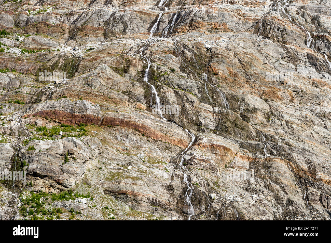 Water streams flowing down canyon wall rock side at exit of Glacier des ...