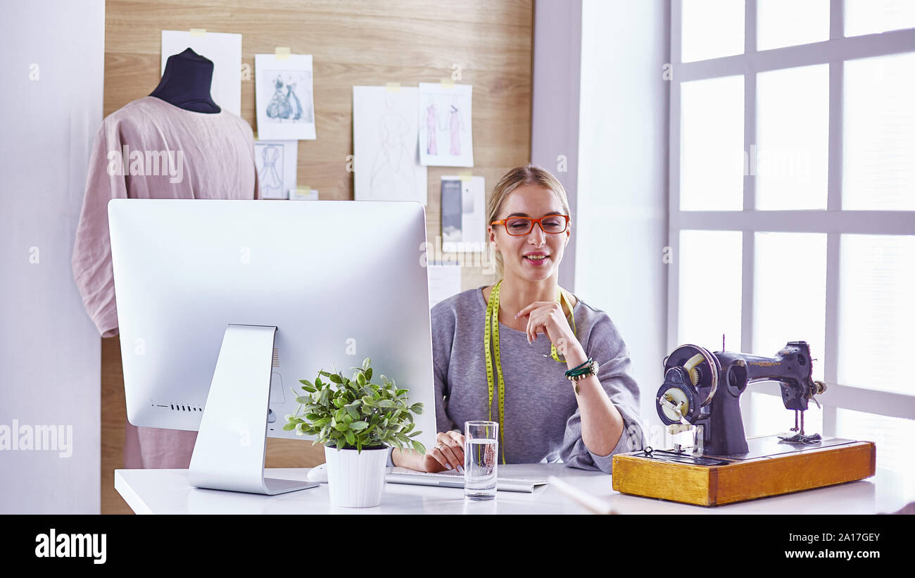 Attractive fashion designer working in office, leaning on desk, drawing ...