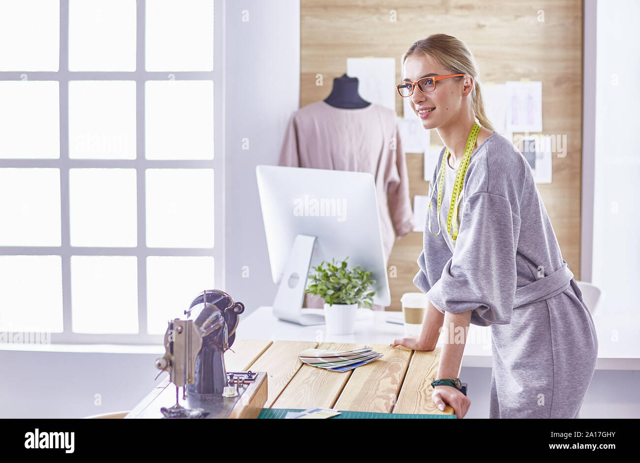 Attractive fashion designer working in office, leaning on desk, drawing ...