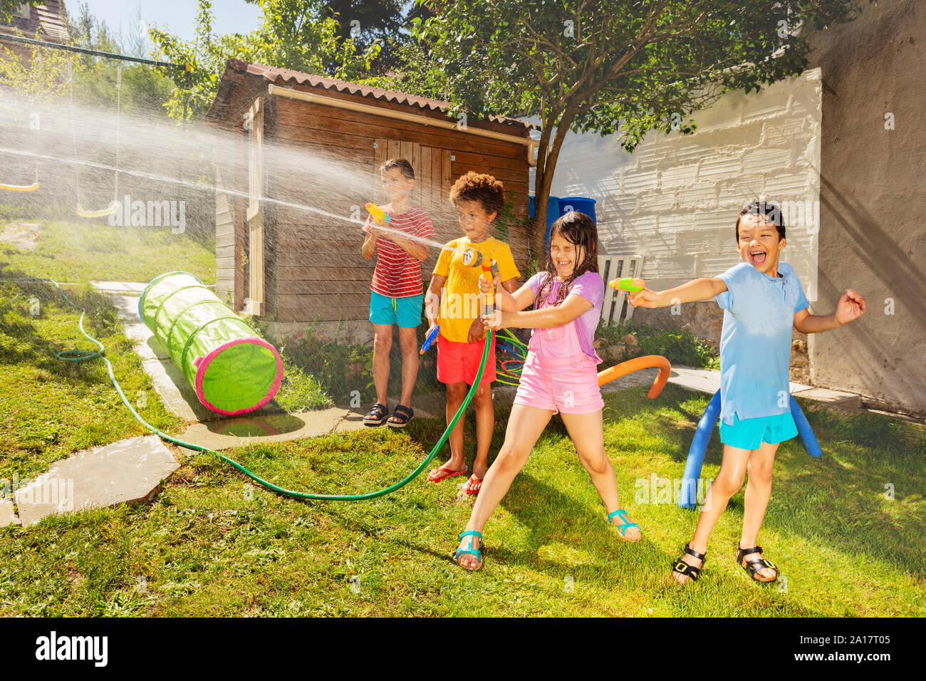 Friends, group of diverse looking children play water gun fight wet ...