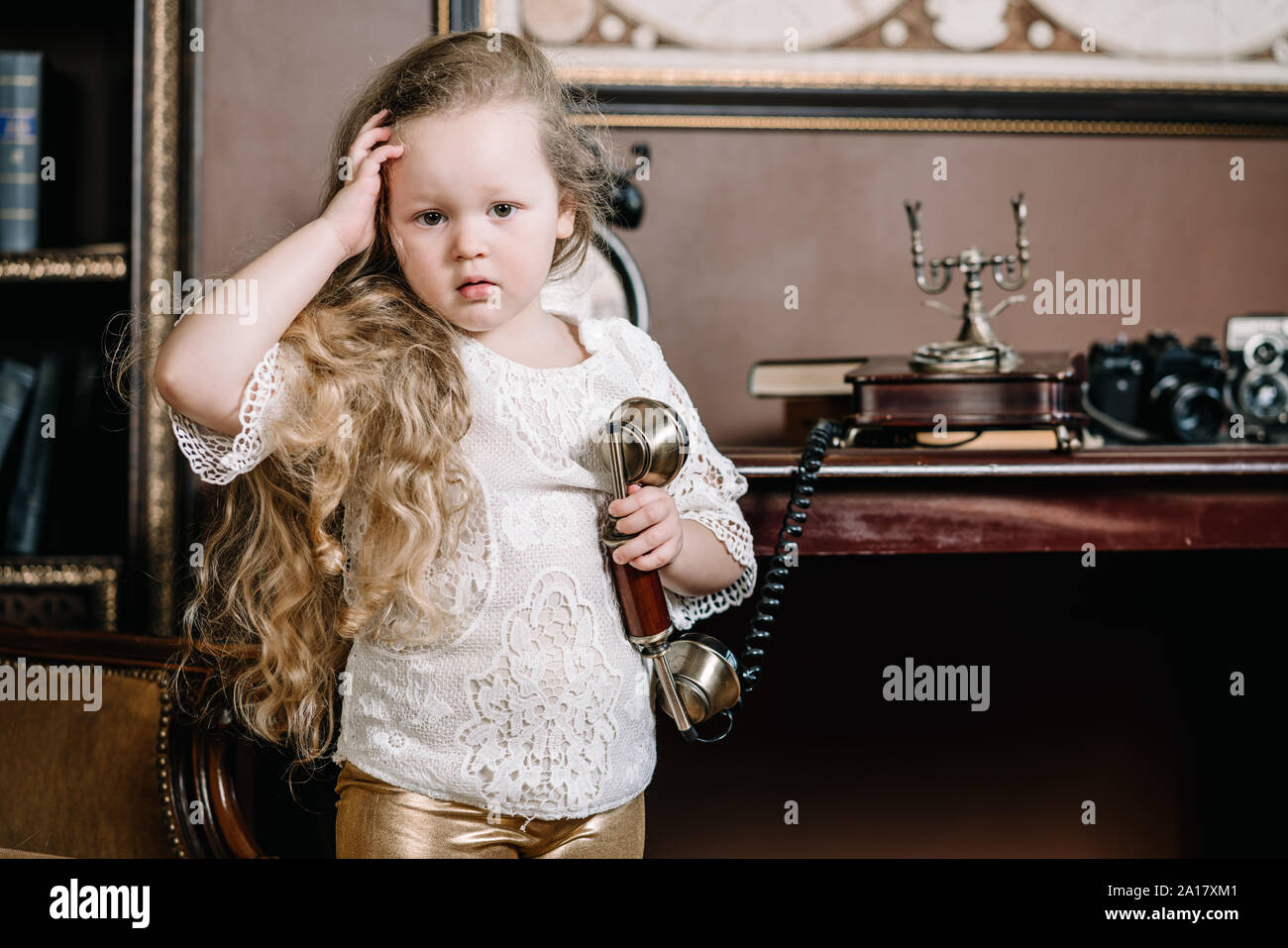Little brooding child girl talking on a retro telephone in the room ...