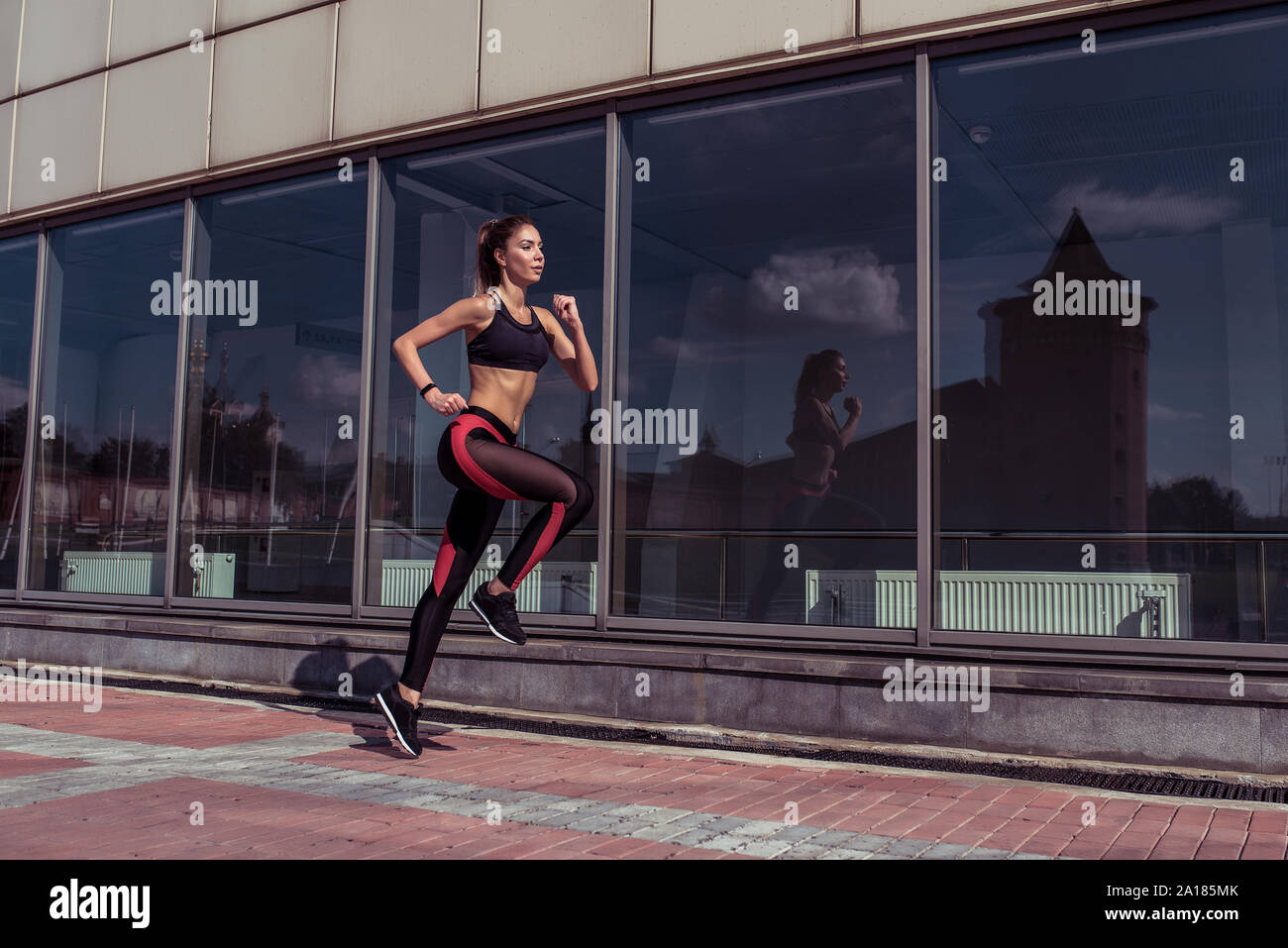Beautiful athletic tanned athlete girl run summer city background glass ...