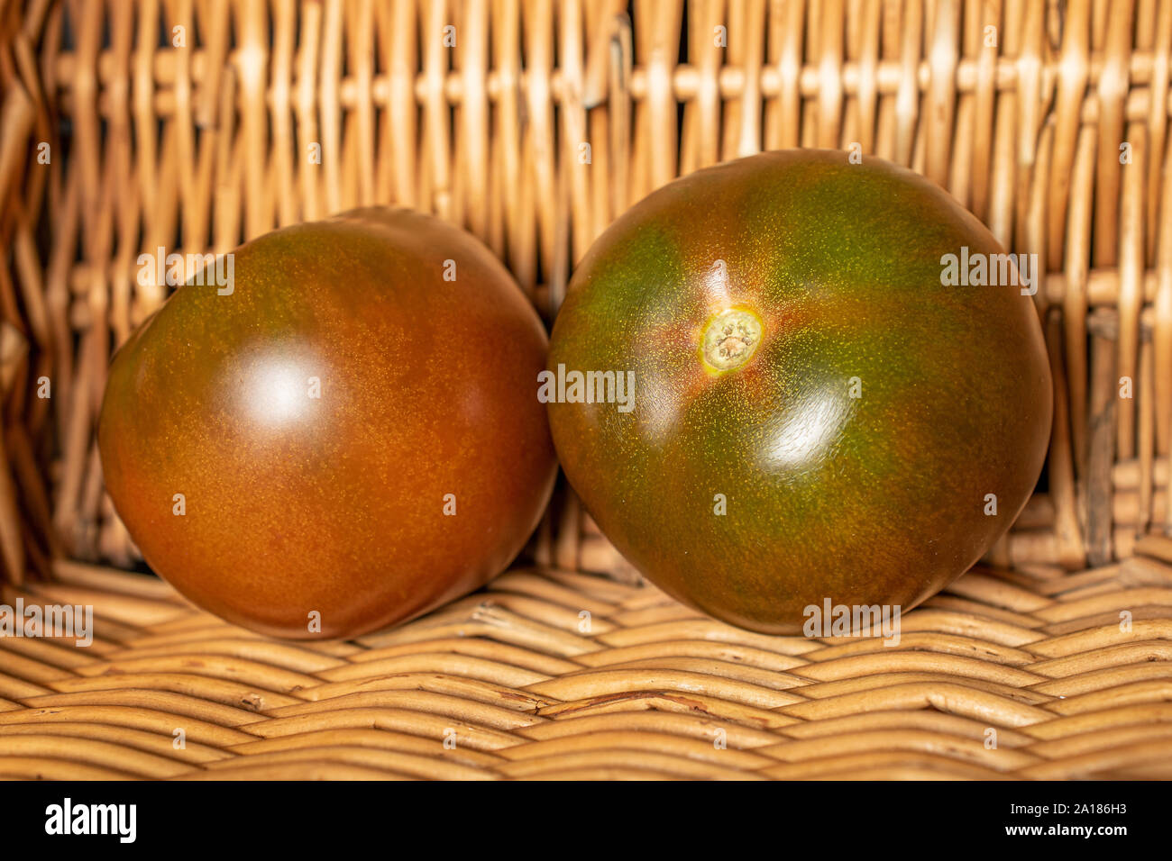 Group of two whole fresh green red tomato with braided rattan behind Stock Photo - Alamy