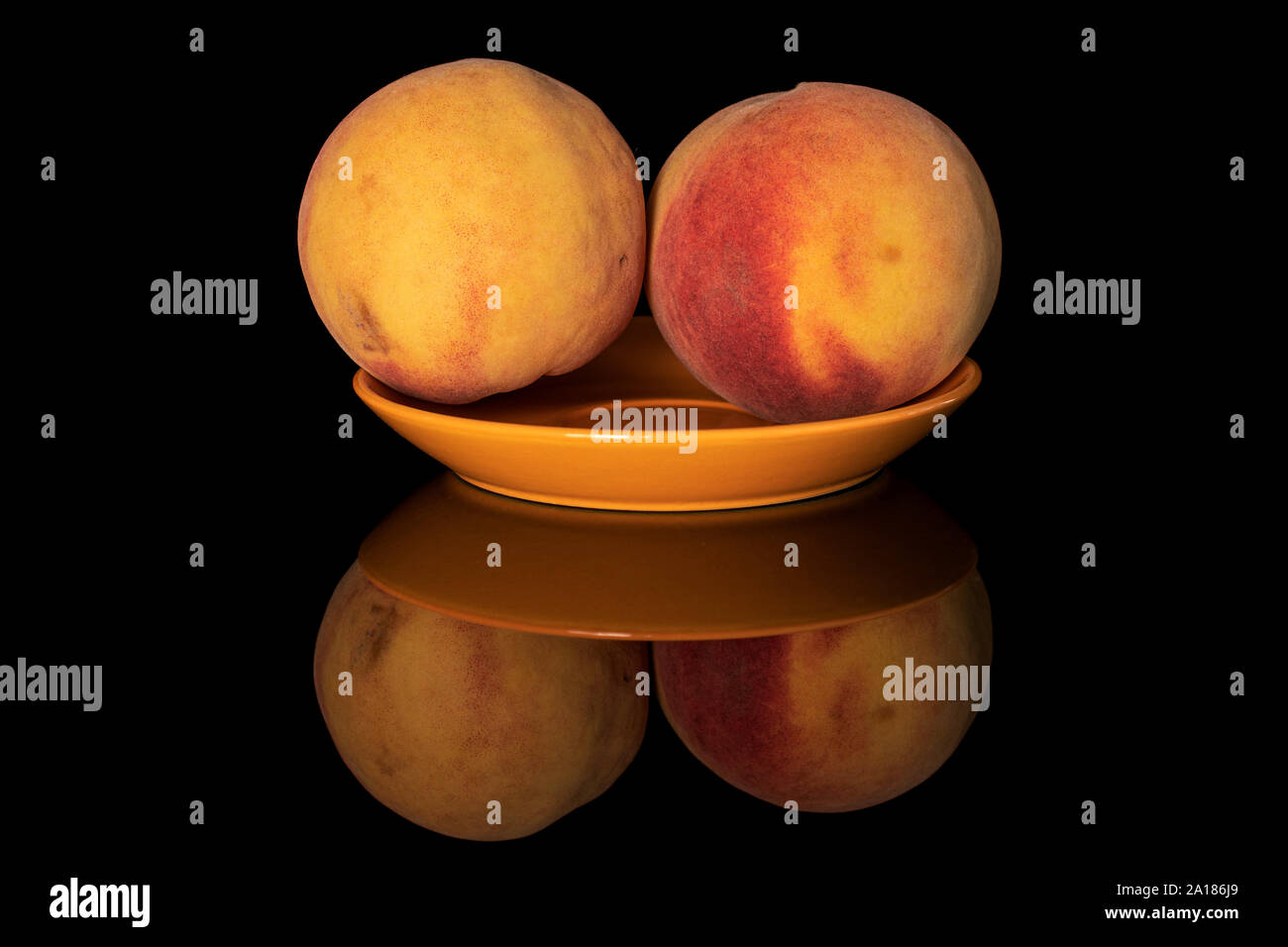 Group of two whole fresh fuzzy peach on orange plate isolated on black ...