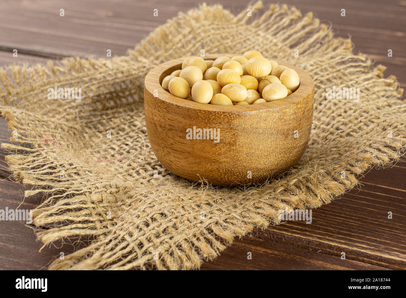 Lot of whole raw yellow soya bean in wooden bowl on jute cloth on brown ...