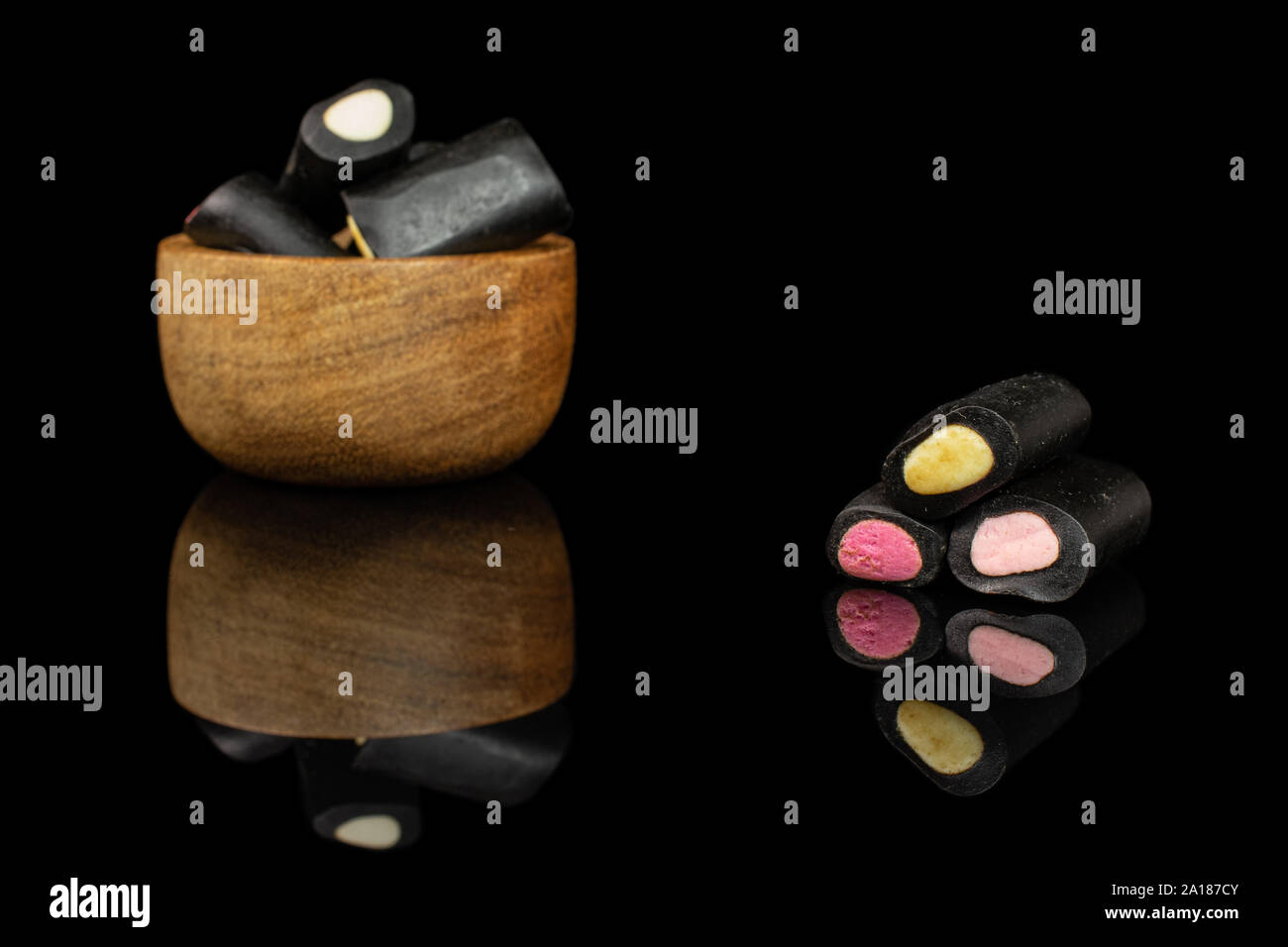 Lot of whole sweet black liquorice candy in tiny wooden bowl isolated ...