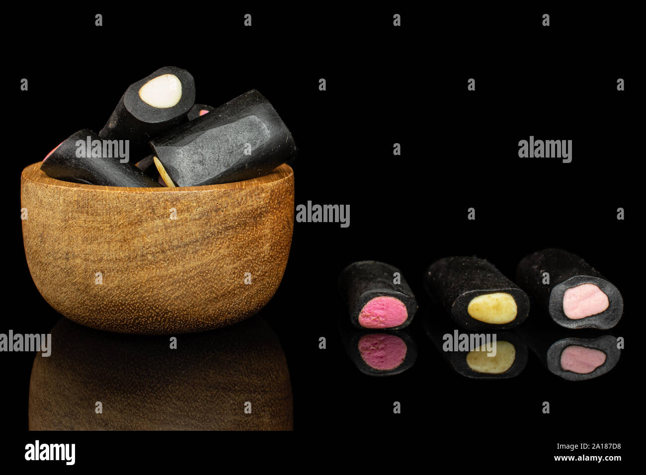 Lot of whole sweet black liquorice candy in tiny wooden bowl isolated ...