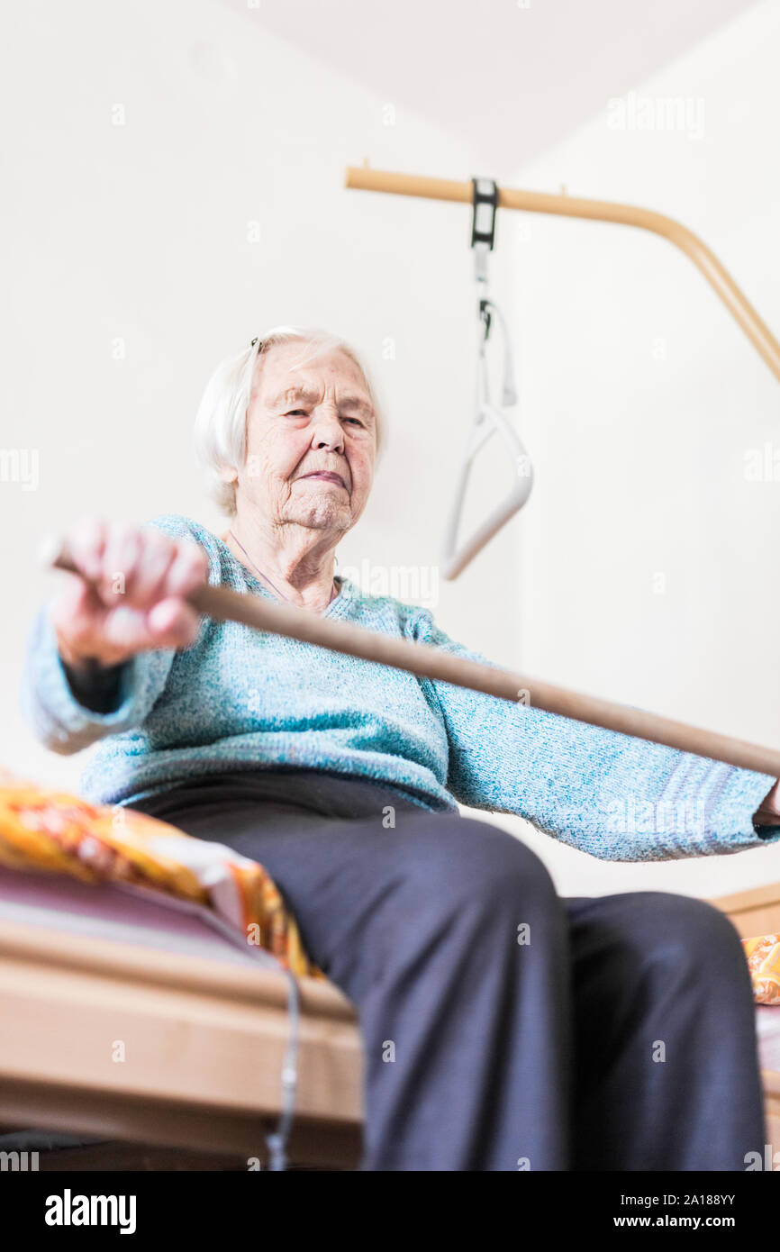 Elderly 96 years old woman exercising with a stick sitting on her bad ...