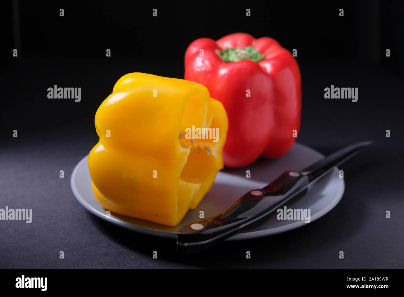 A sliced yellow bell pepper and whole red bell pepper together on small ...