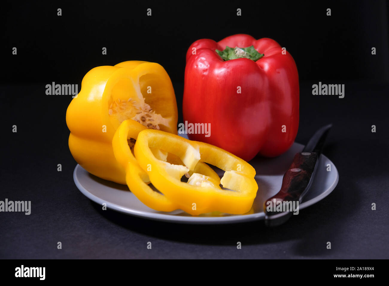 A sliced yellow bell pepper and whole red bell pepper together on small ...