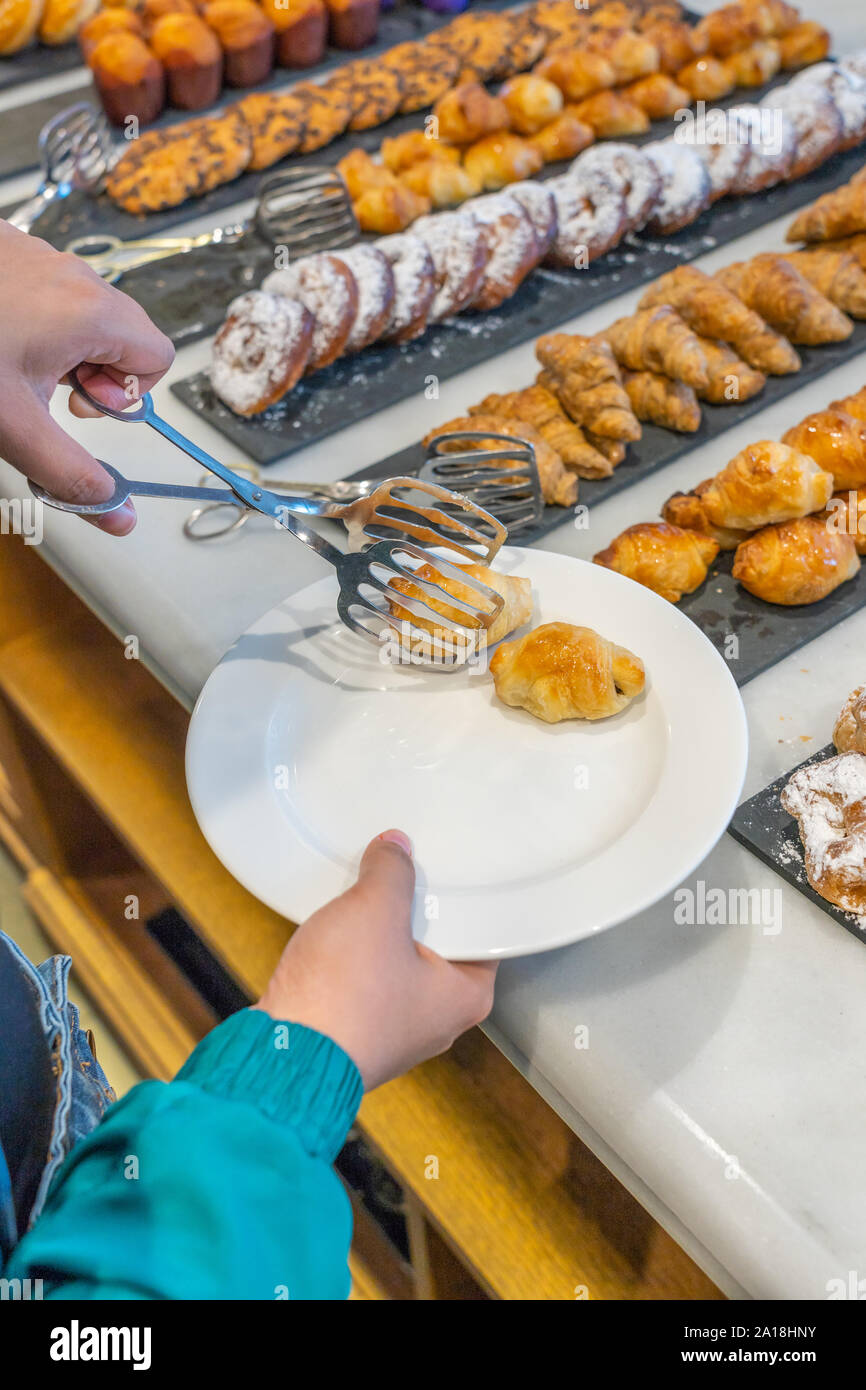 Vertical photo of woman using tongs and selecting pastry croissant ...