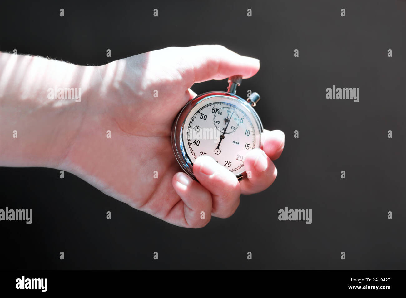 Hand holding a stopwatch and pressing the button to note the time. Dark ...