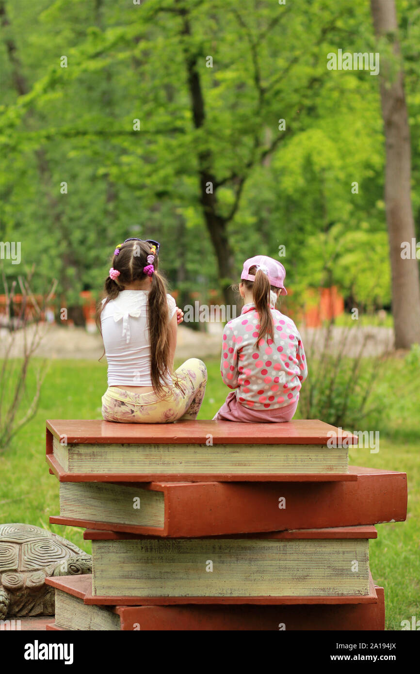 Two girls sitting on pile of giant books in the park, back view Stock ...