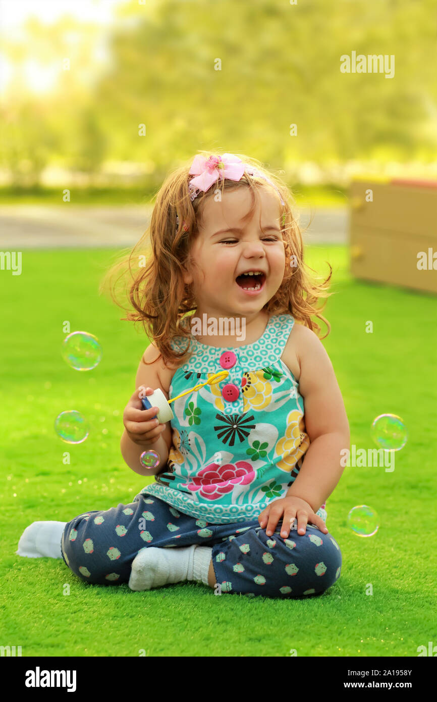 Laughing one year old girl learning to blow soap bubbles and having fun ...