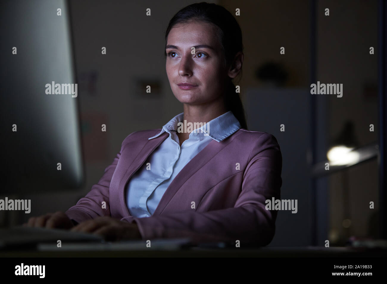 Young beautiful secretary sitting at the table looking at computer ...
