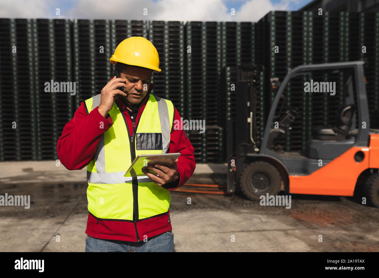 Forklift driver using smartphone and tablet outside factory warehouse ...