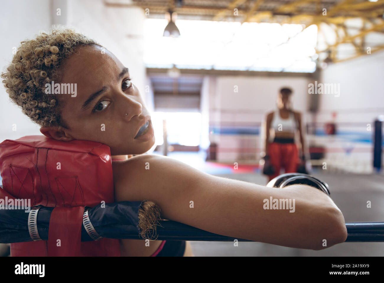 Female boxer looking at camera while resting in boxing ring at fitness ...