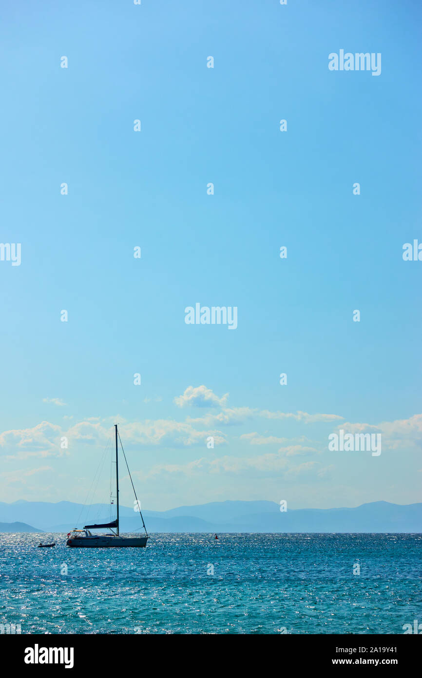 Single sail yacht in the sea near islands and blue sky with clouds ...
