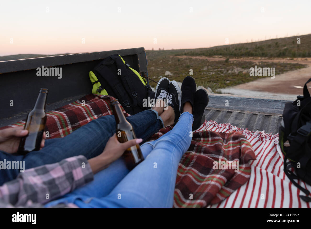 Legs of a young couple on a road trip sitting outside on their truck ...