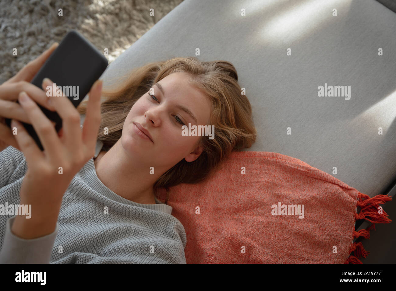 Young blonde woman lying down using smartphone Stock Photo - Alamy