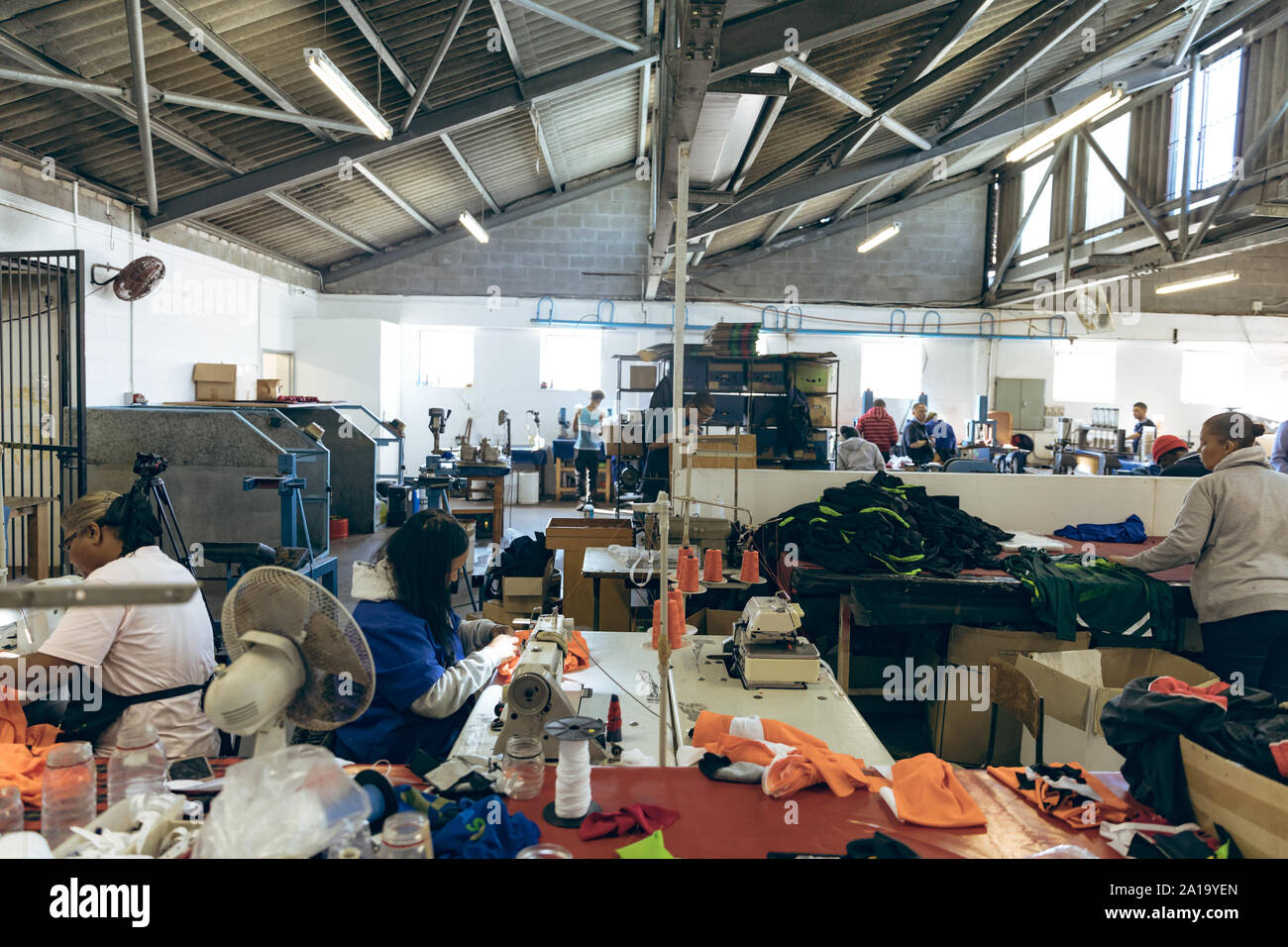 Women using sewing machines and sorting fabric in a clothing factory ...