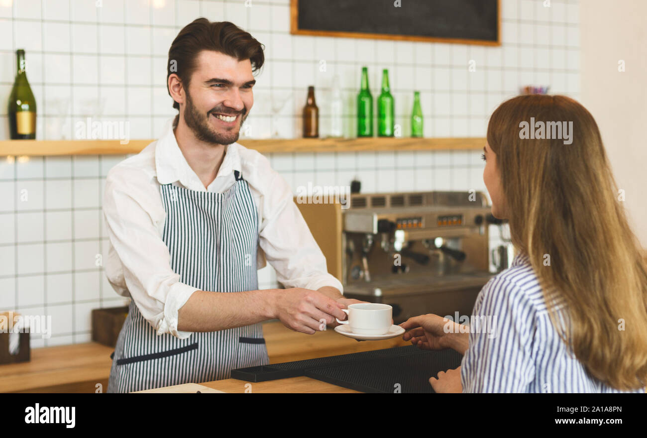 Waiter giving aromatic coffee to girl and widely smiling to her Stock ...