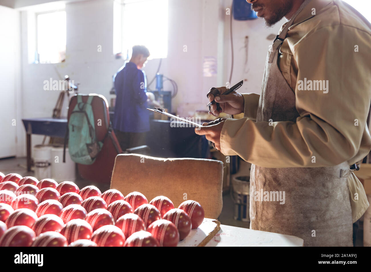 Young man writing on clipboard at a cricket ball factory Stock Photo ...