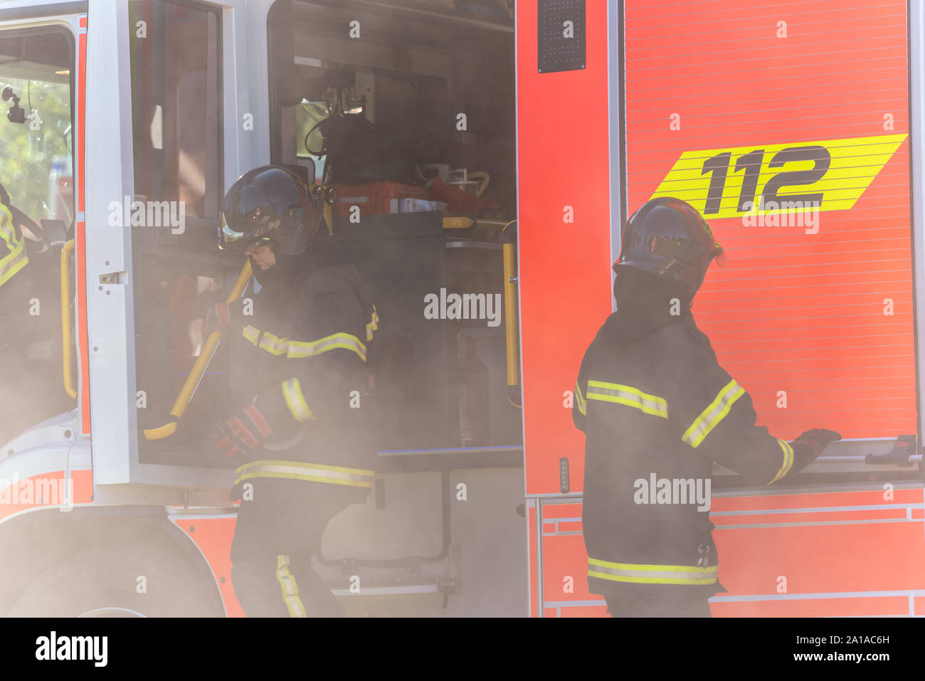 Firefighters in suit and helmet jumping out of a fire truck ...