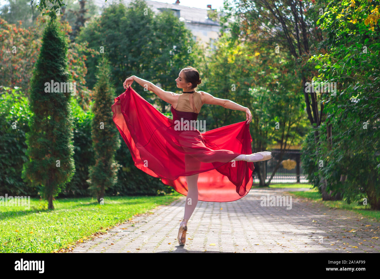 Woman ballerina in red ballet dress dancing in pointe shoes in autumn ...