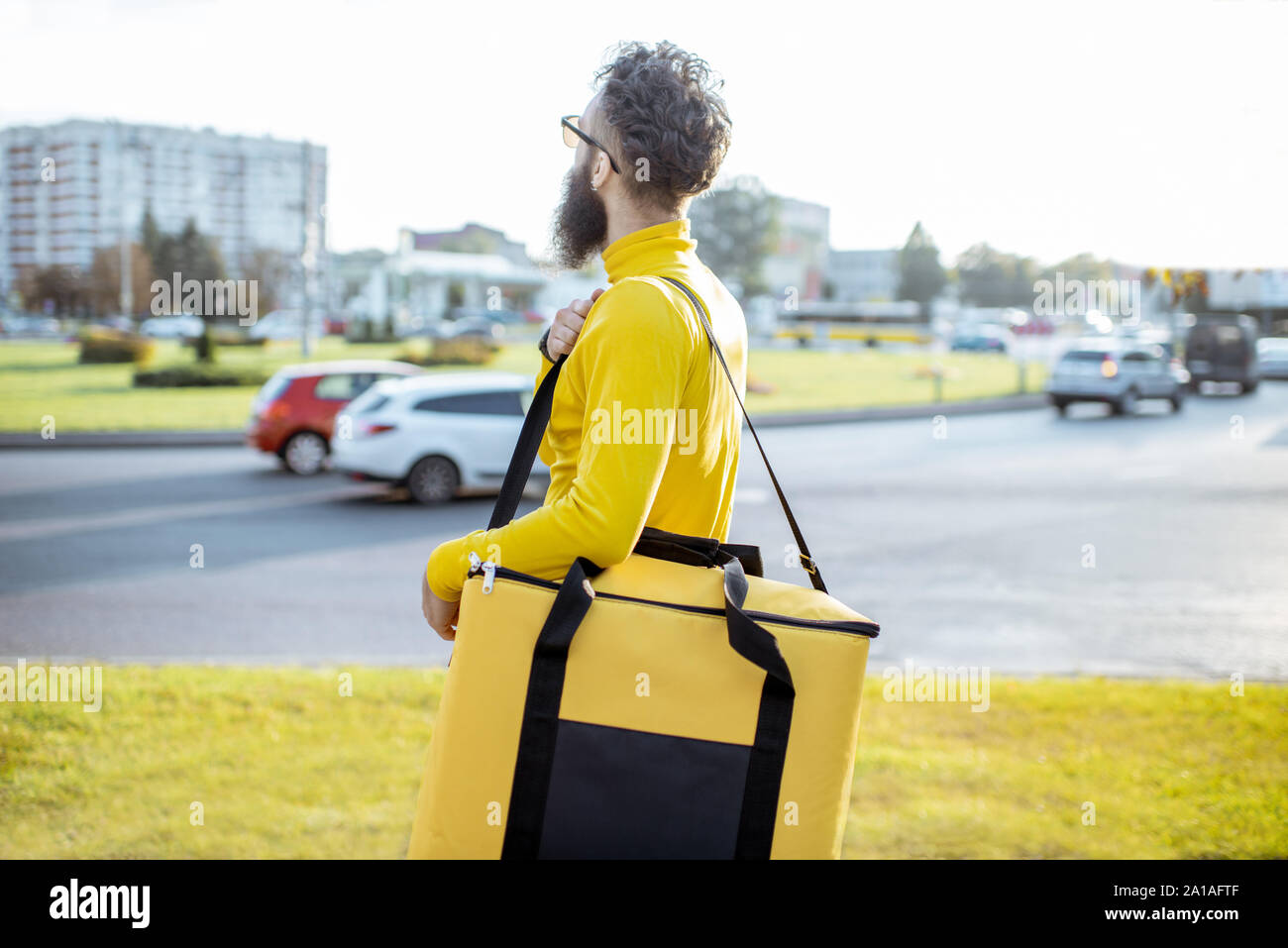 Young courier delivering food, walking with yellow thermal bag on the ...