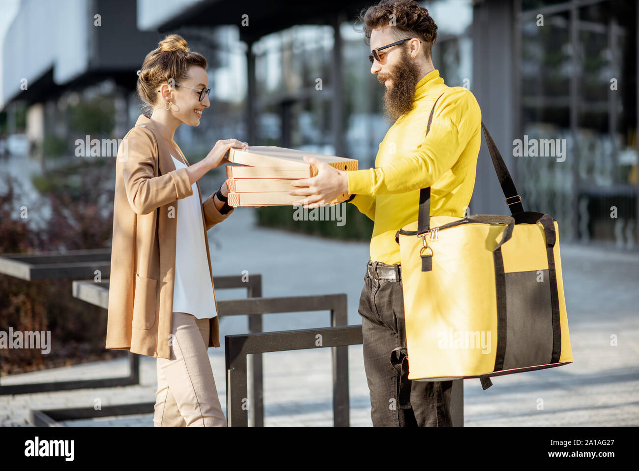 Male courier delivering pizza with thermal bag to a young businesswoman ...