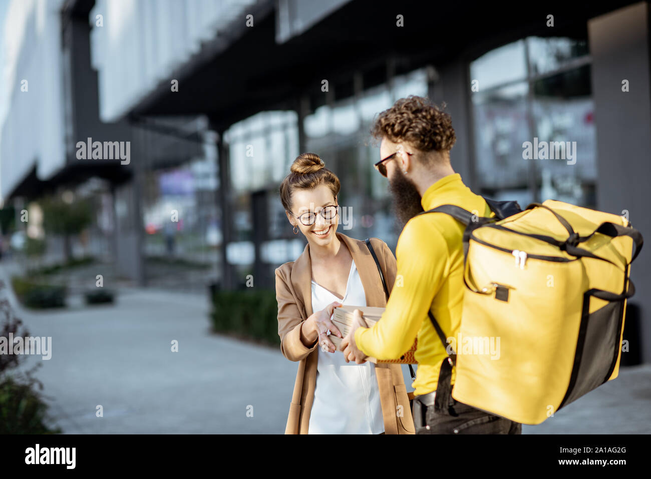 Male courier delivering pizza with thermal bag to a young businesswoman ...