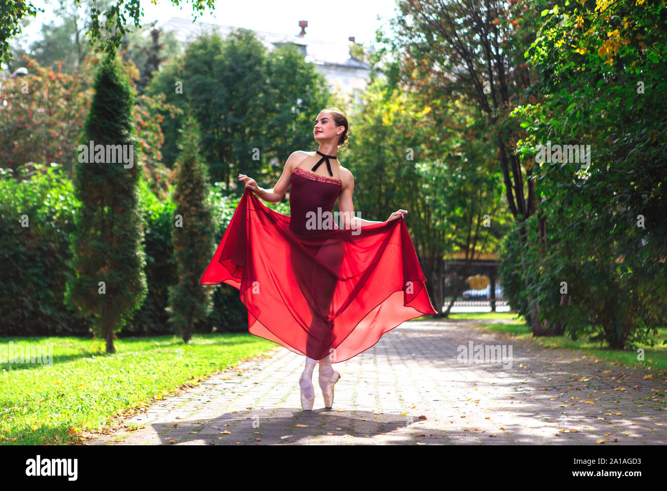 Woman ballerina in red ballet dress dancing in pointe shoes in autumn ...