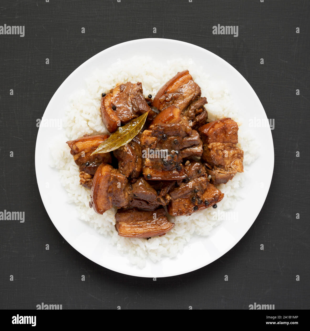 Homemade Filipino Adobo Pork with rice on a white plate on a black ...