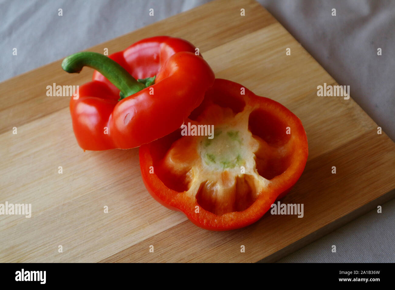 Red capsicum pepper cut in half on wood chopping board Stock Photo - Alamy