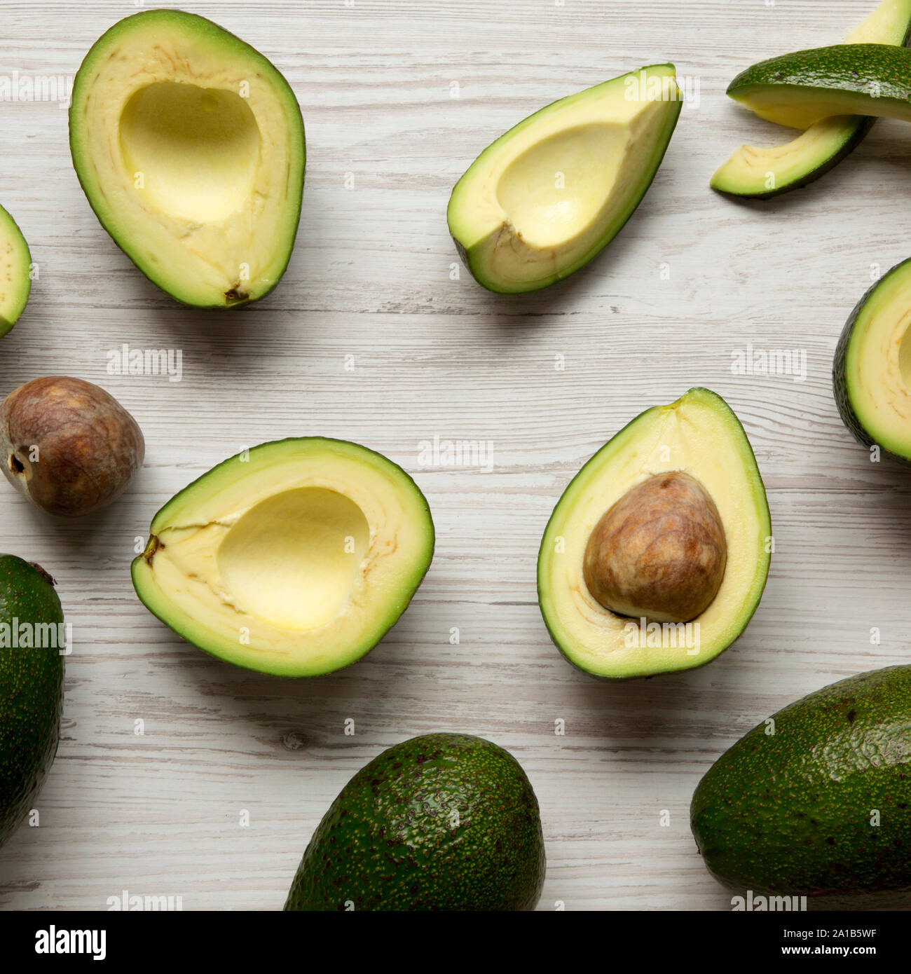 Whole and chopped avocados on a white wooden background, view from ...