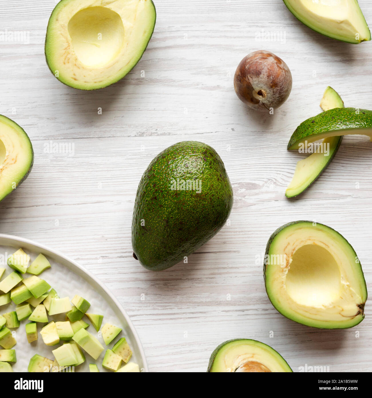 Whole and chopped avocados on a white wooden surface, top view ...