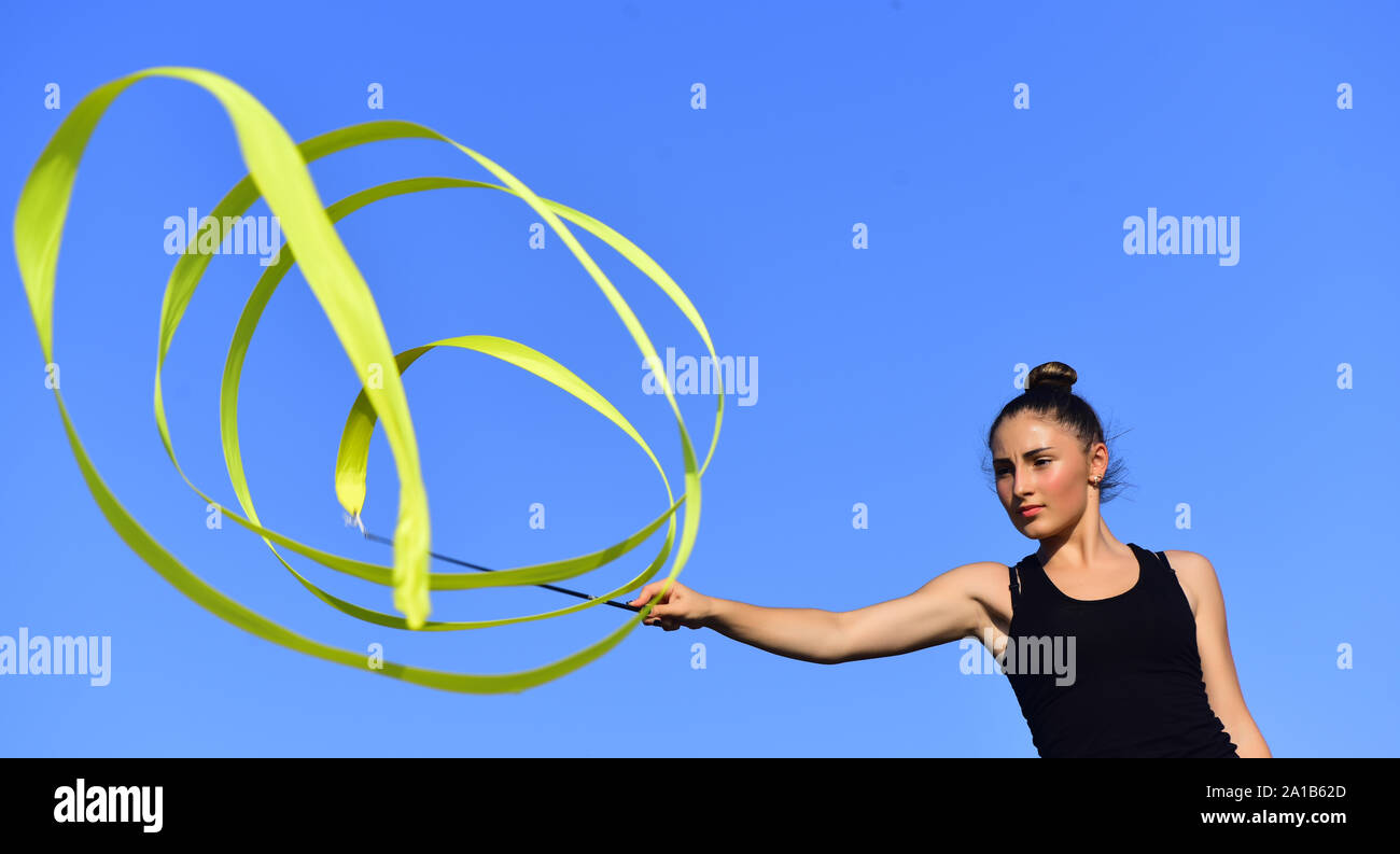 Woman gymnast in black sportswear swirl green ribbon on blue sky ...