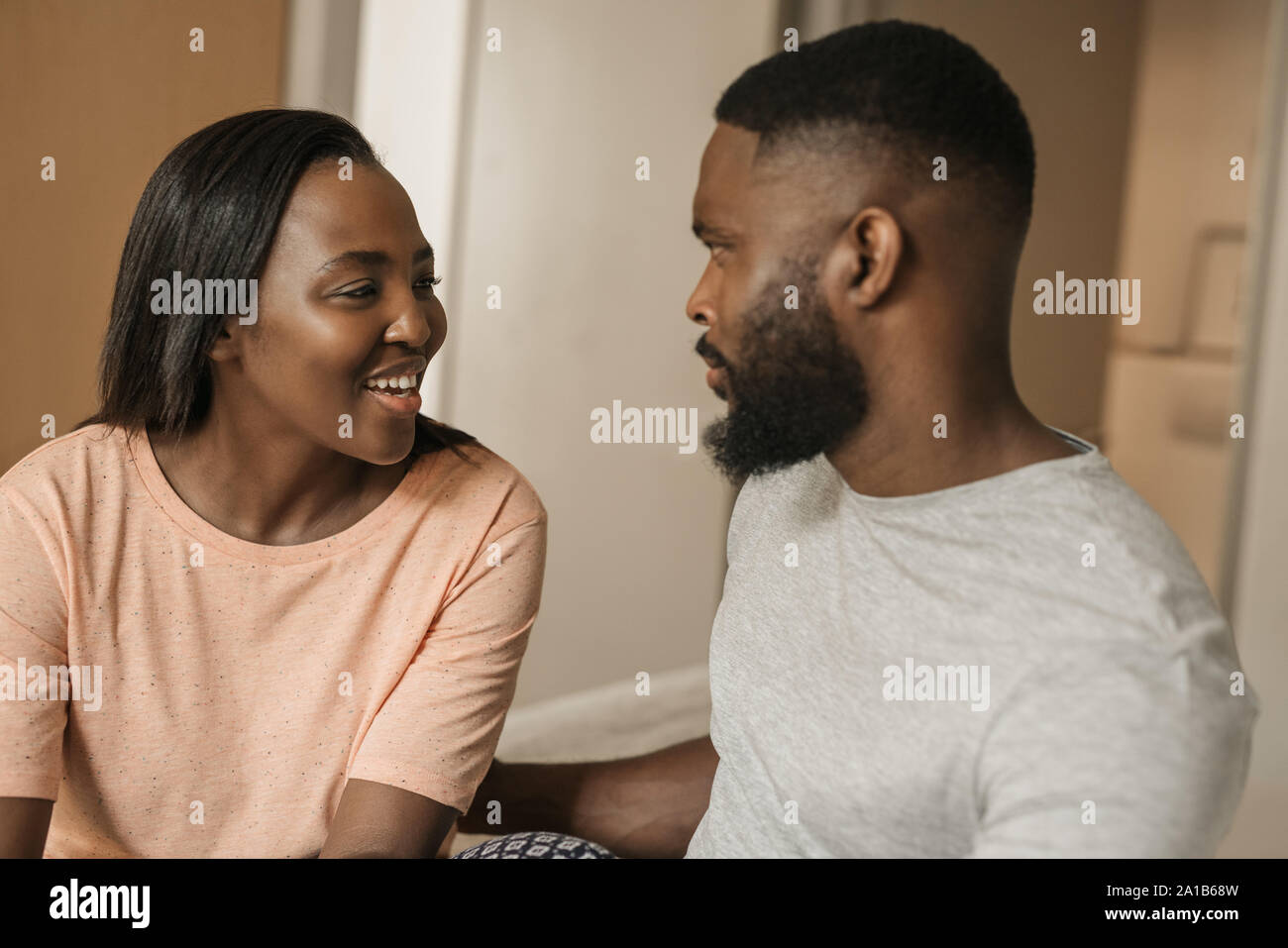 Smiling young African American couple talking together on their bed ...