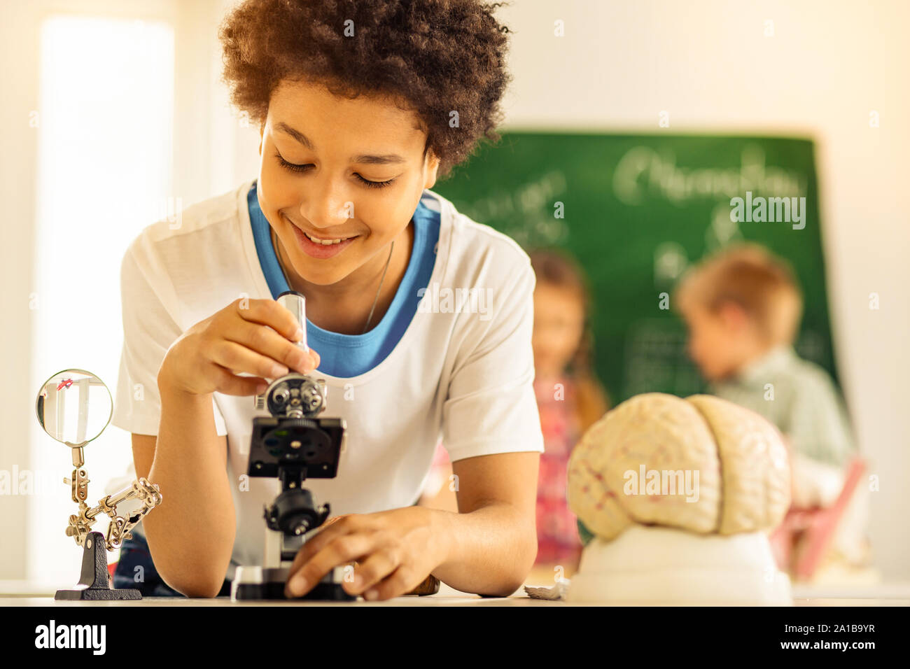 Pleased brunette kid looking through the microscope Stock Photo - Alamy