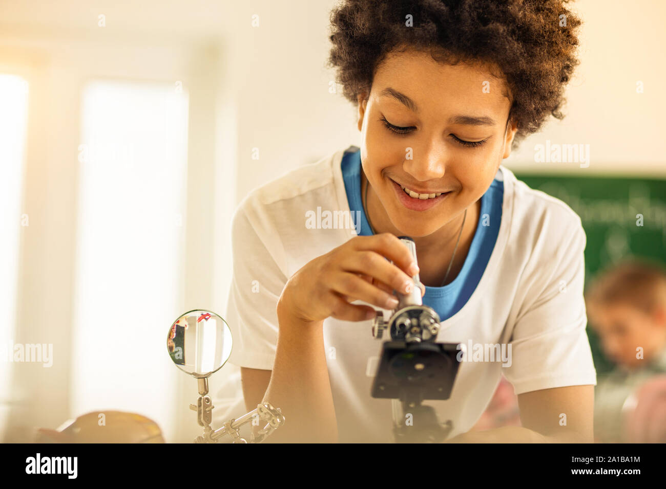 Joyful teenager using microscope while preparing for lesson Stock Photo - Alamy