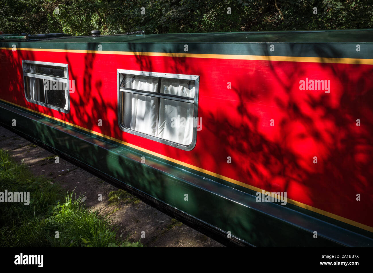 Red and green narrowboat with tree branched casting a shadow Stock ...