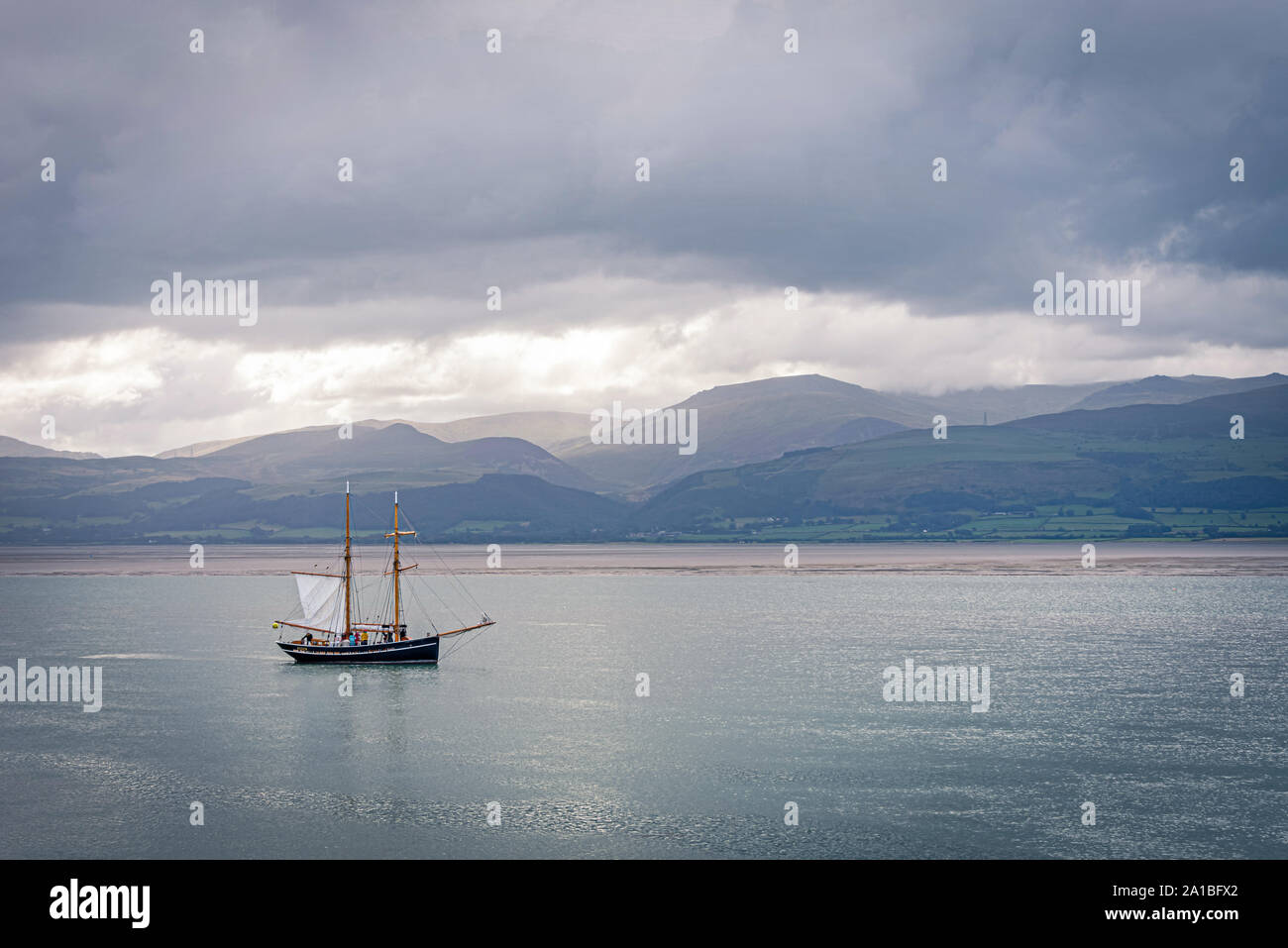 The Menai Strait at Beaumaris. A sailing ship manoeuvres against a ...