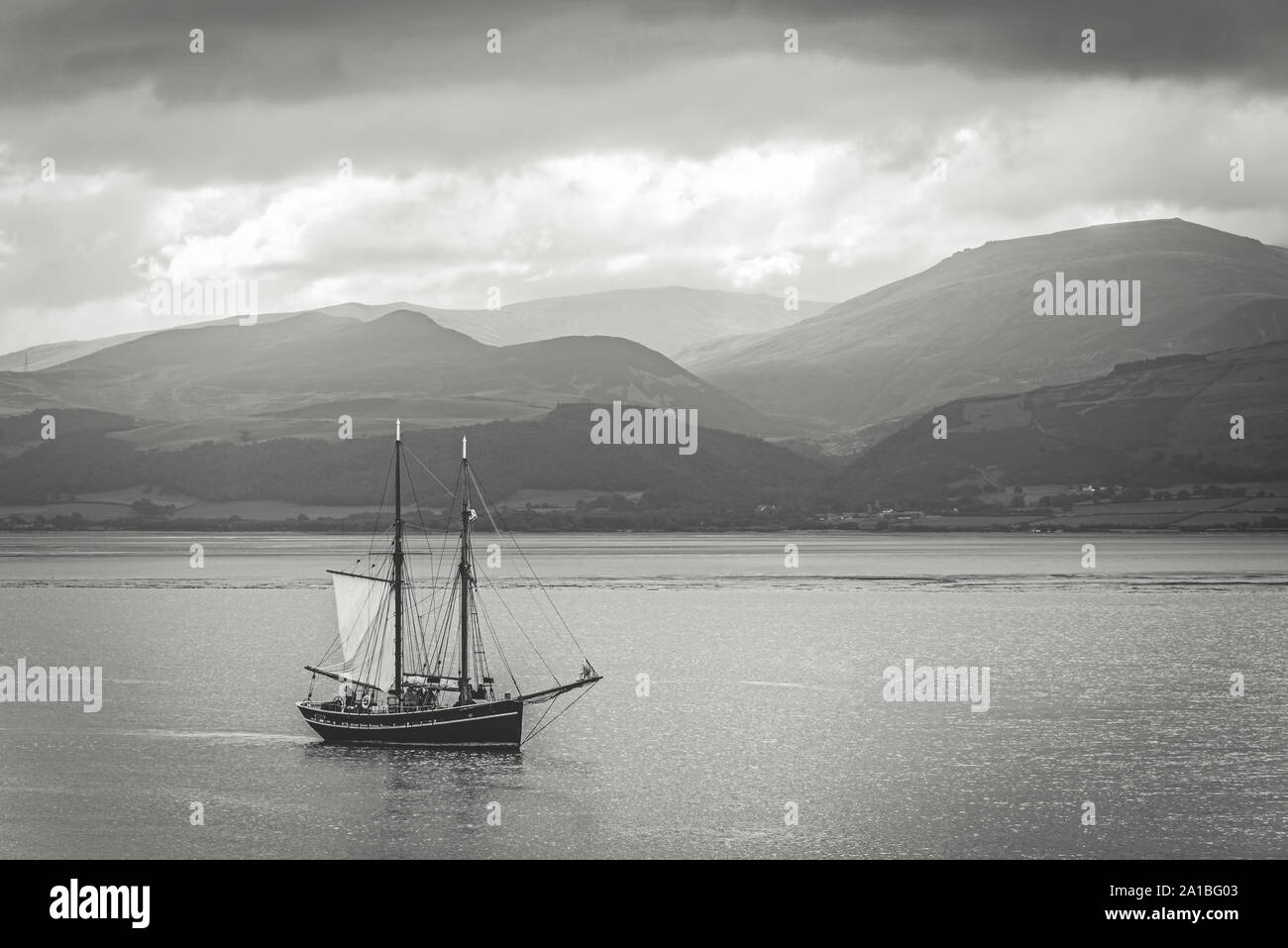 The Menai Strait at Beaumaris. A sailing ship manoeuvres against a ...